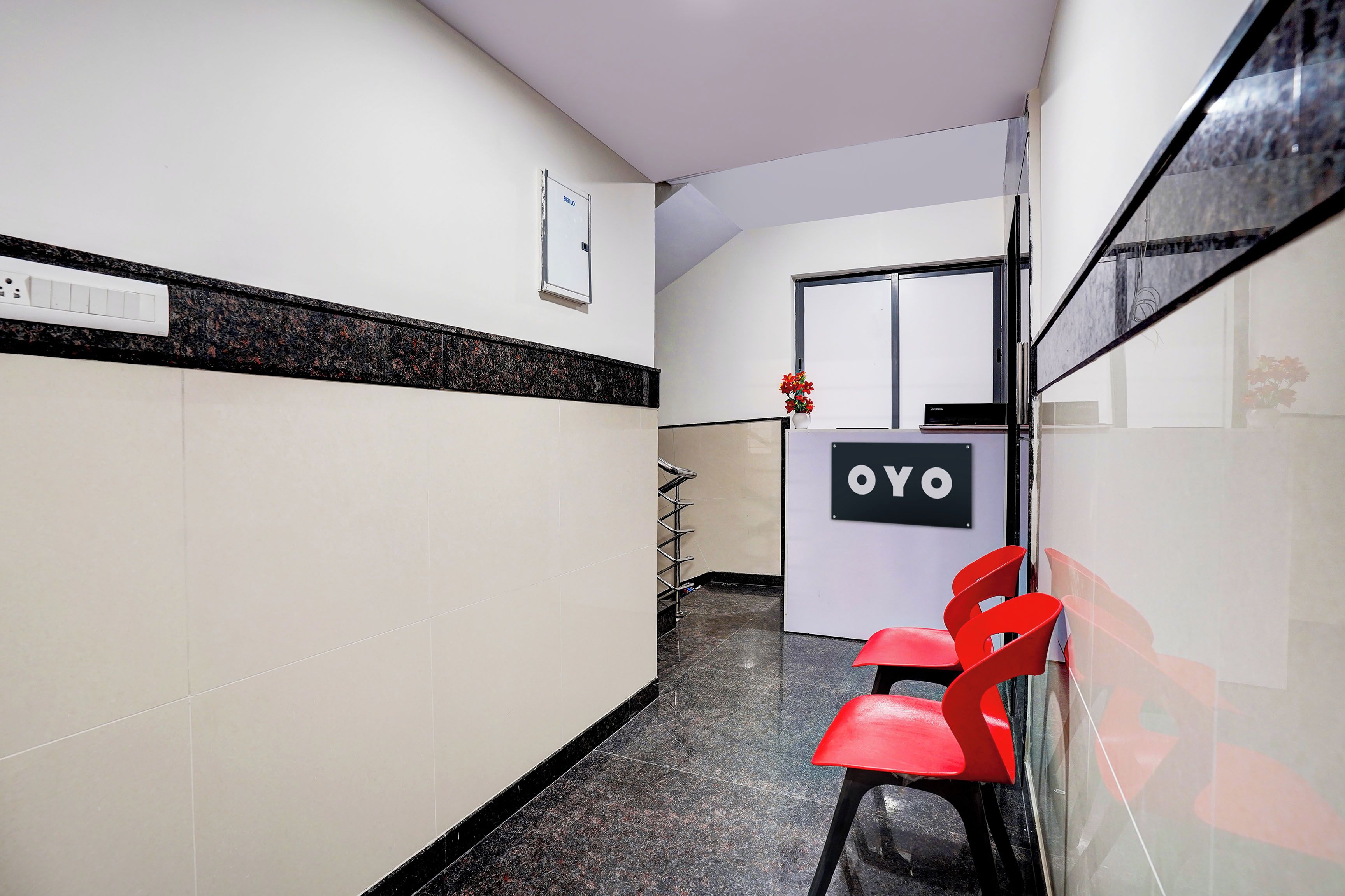 Um corredor com uma mesa de recepção, uma placa indicando 'OYO' e cadeiras vermelhas.