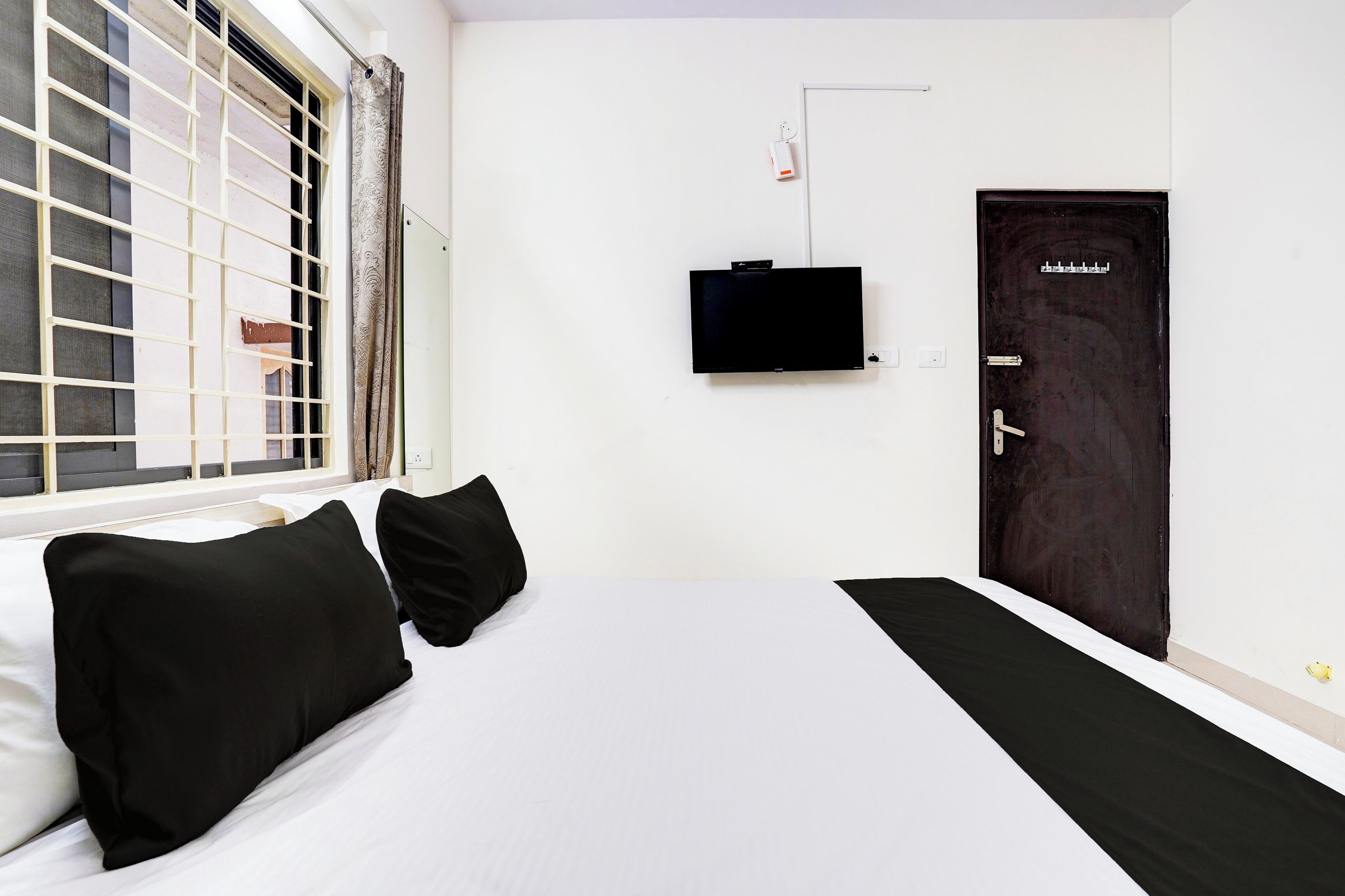 Quarto de hotel com cama, televisão na parede, porta e janela com vista.