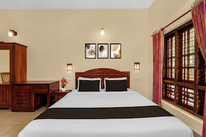 Quarto de hotel com uma cama grande, cabeceira de madeira, mesas de cabeceira, escrivaninha e janela com cortinas.