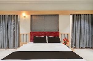 Quarto de hotel com uma cama grande, cabeceira vermelha, cortinas cinzas e uma janela com vista.