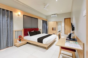 Quarto de hotel com cama, mesa de cabeceira, escrivaninha com chaleira, cadeira, espelho e ar-condicionado.