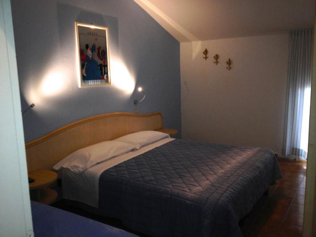 Quarto com cama, mesa de cabeceira, luminária na parede e um pôster.