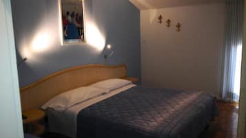 Quarto com cama, mesa de cabeceira, luminária na parede e um pôster.