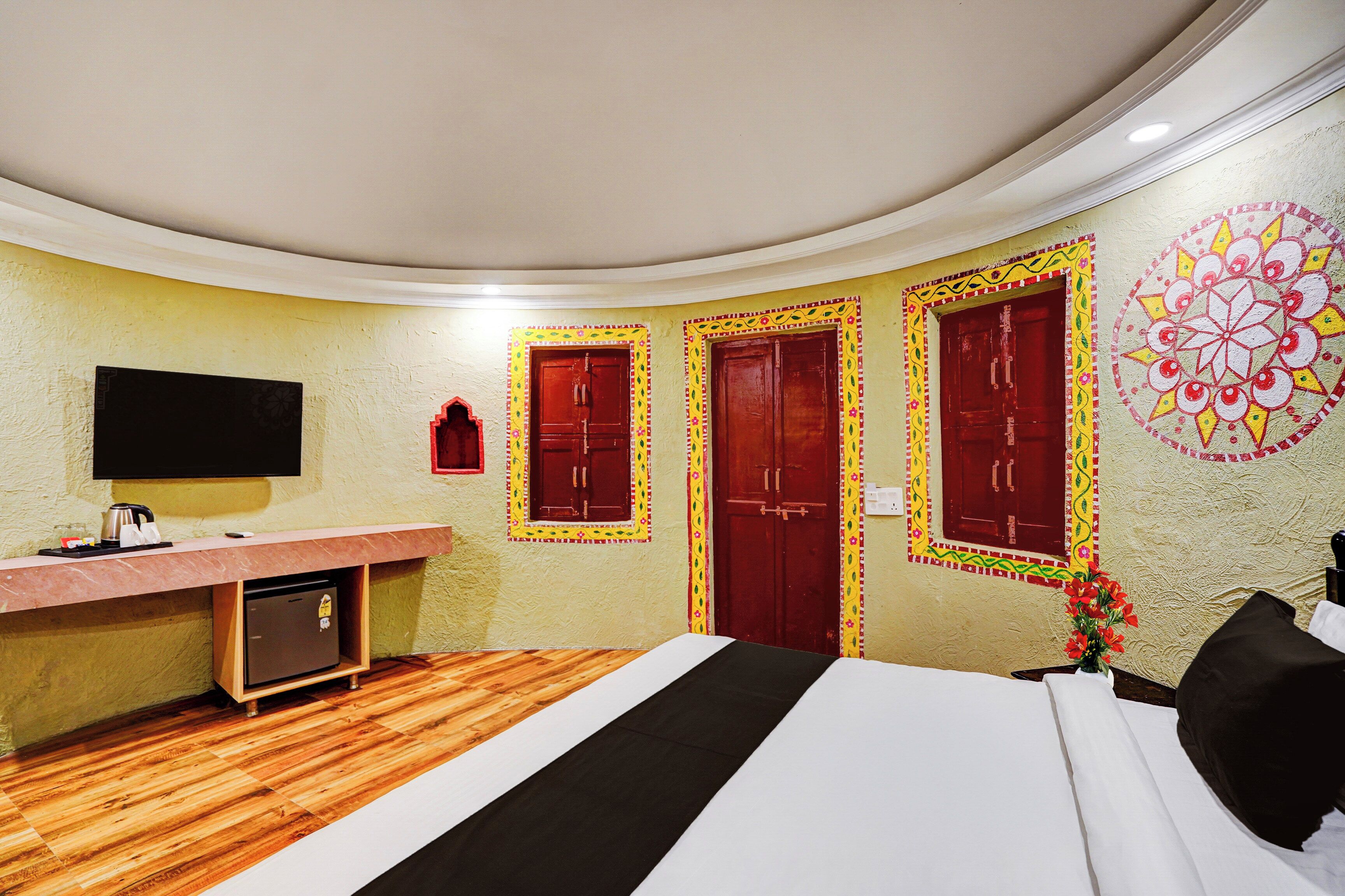 Quarto de hotel com cama, escrivaninha, televisão de tela plana, frigorífico e parede com padrão decorativo.