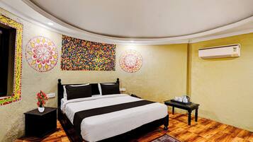 Quarto de hotel com cama, mesas de cabeceira, ar condicionado e arte decorativa na parede.