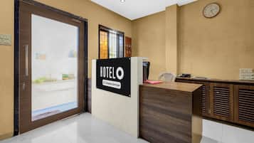 Uma área de recepção de hotel com balcão, relógio e janela com vista para o exterior.