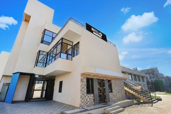 Um hotel moderno com uma placa de destaque, uma escadaria que leva à entrada e um céu azul claro.