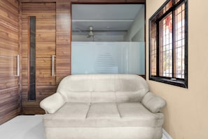 Quarto com sofá, guarda-roupa de madeira, janela com persianas e ventoinha no teto.