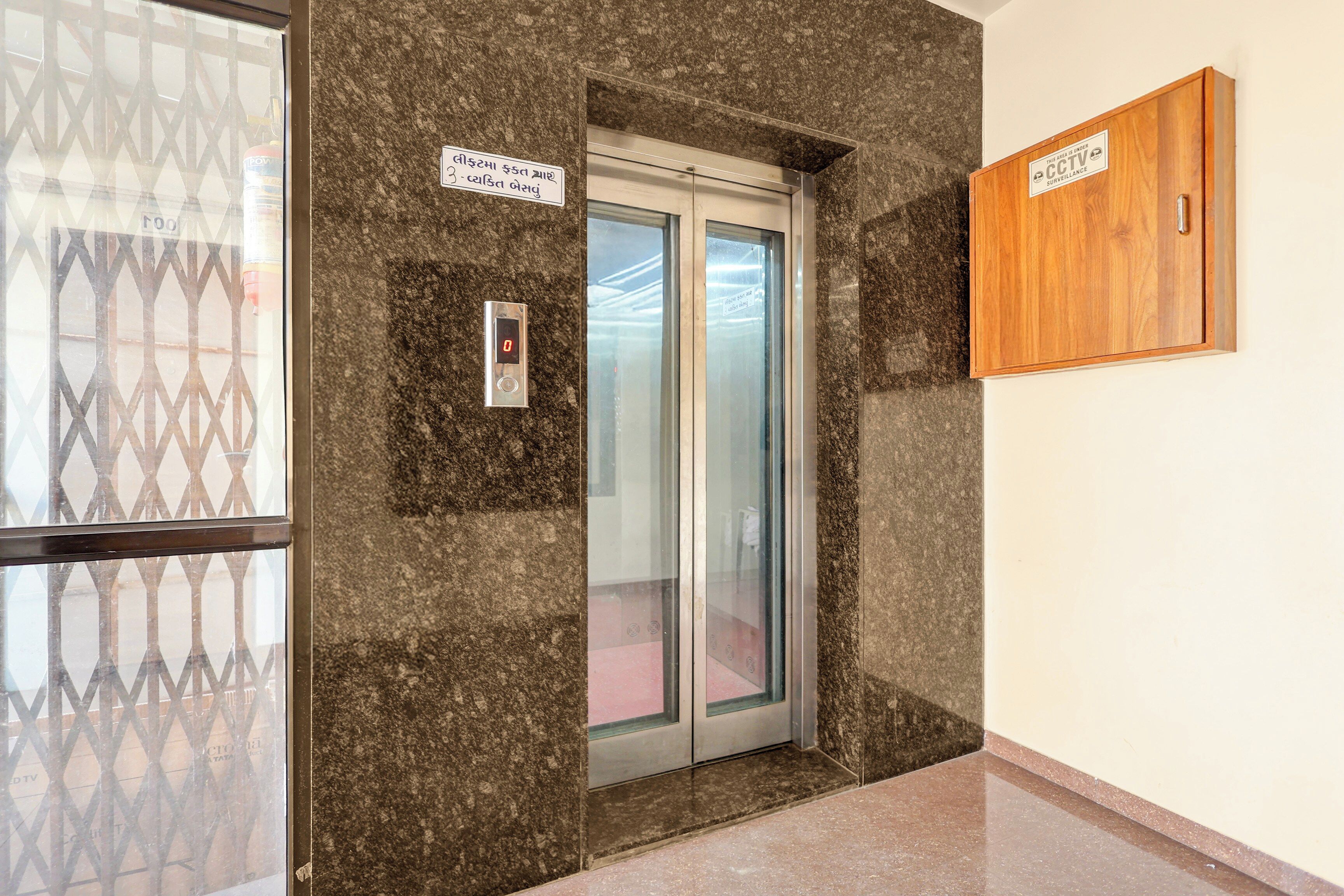 Um elevador com mostrador digital, aviso indicando vigilância por câmeras de segurança e um armário de madeira.