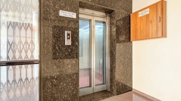 Um elevador com mostrador digital, aviso indicando vigilância por câmeras de segurança e um armário de madeira.