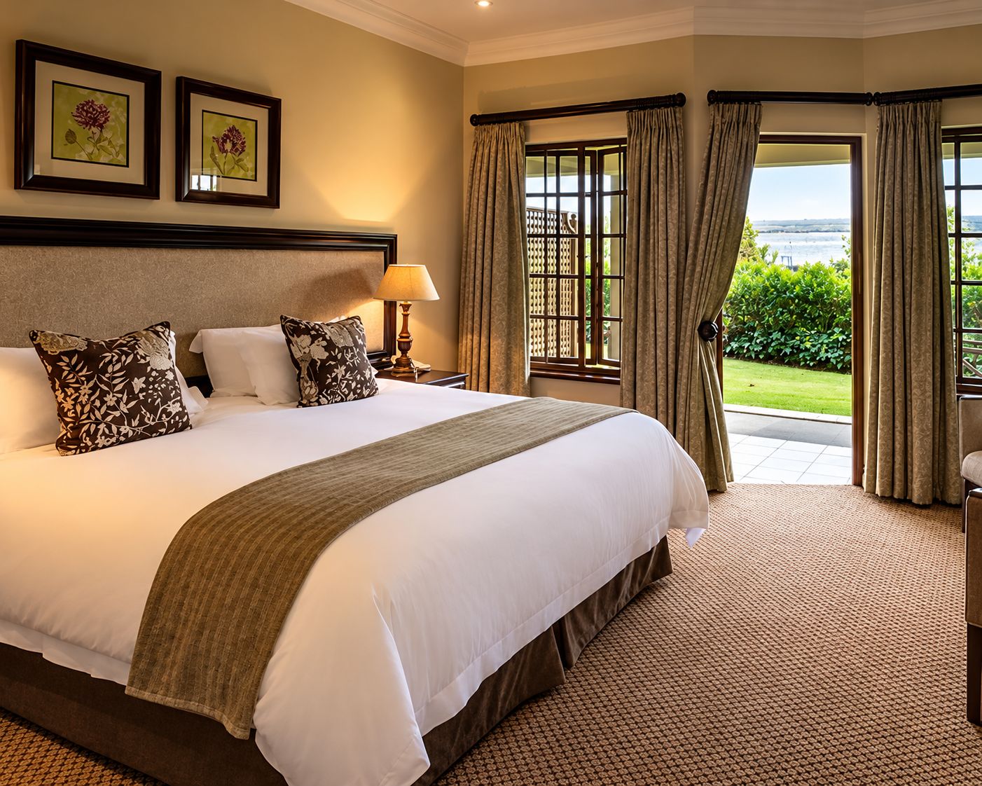 Quarto de hotel com uma cama grande, mesa de cabeceira, luminária e vista para o exterior.
