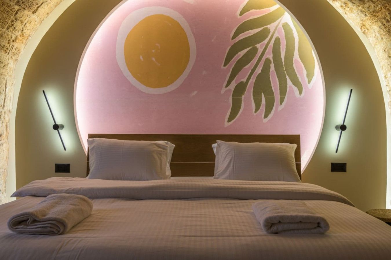 Quarto de hotel com cama, almofadas e parede com um desenho circular.