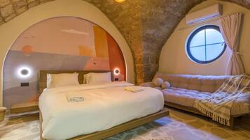 Quarto aconchegante com cama, sofá e janela redonda.