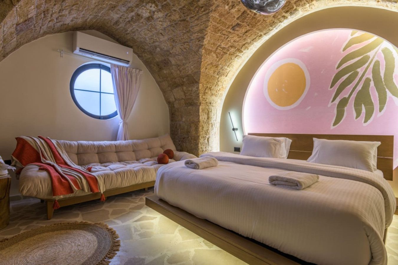 Quarto aconchegante com teto de pedra, janela redonda e cama com almofadas e cobertor.