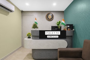 Bancada de recepção com uma placa indicando 'PALETTE' e 'OYO-Serviced'. Há duas plantas em vasos e duas bandeiras na parede atrás do balcão.