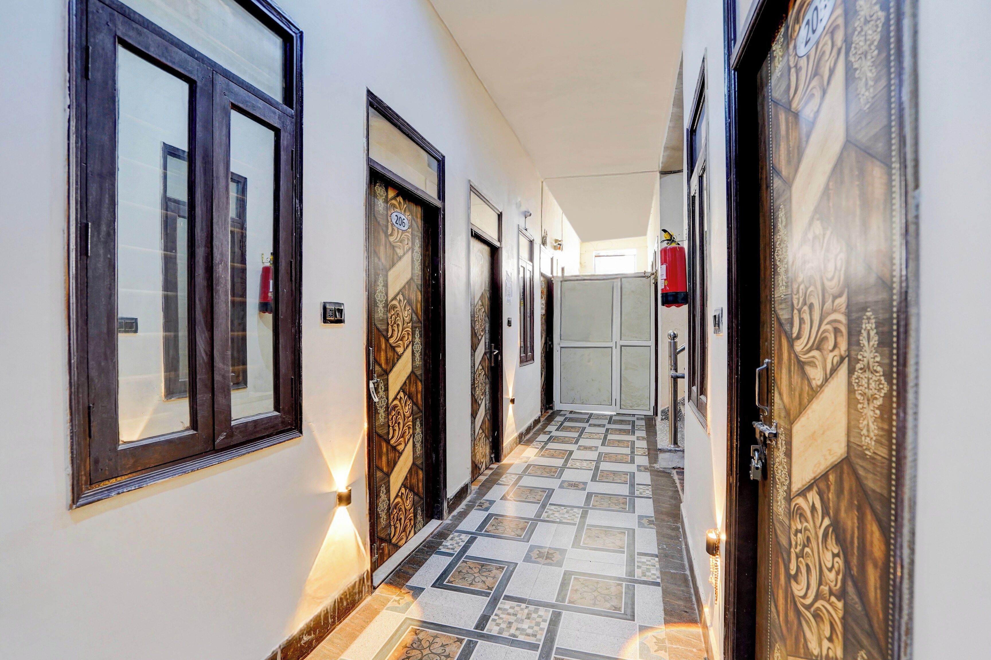 Um corredor com piso de azulejos estampados, portas de madeira com detalhes decorativos e um extintor de incêndio fixado na parede.