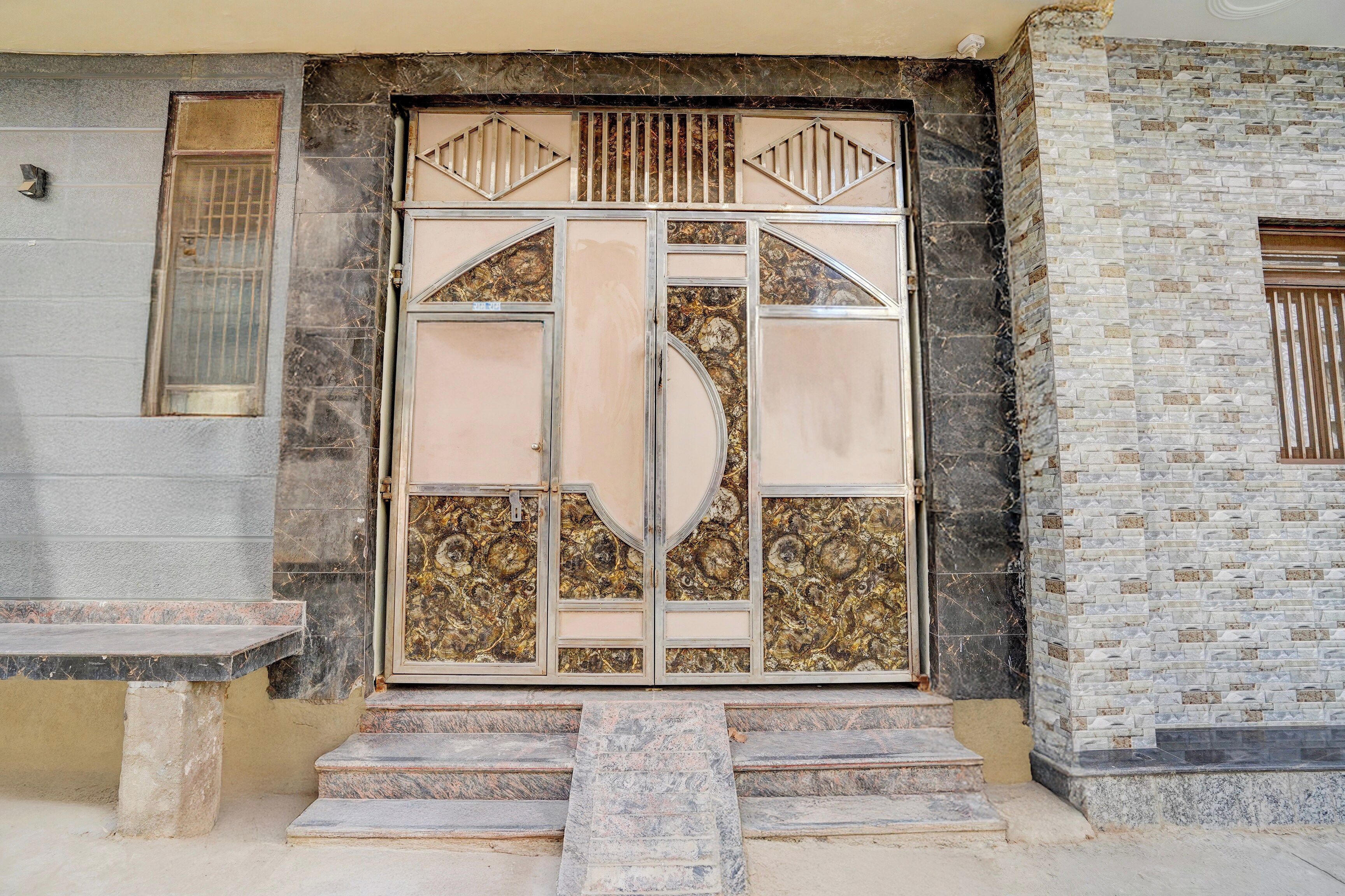 Entrada de um edifício com um portão de metal decorativo, degraus que conduzem a ele e uma parede com uma janela à esquerda.