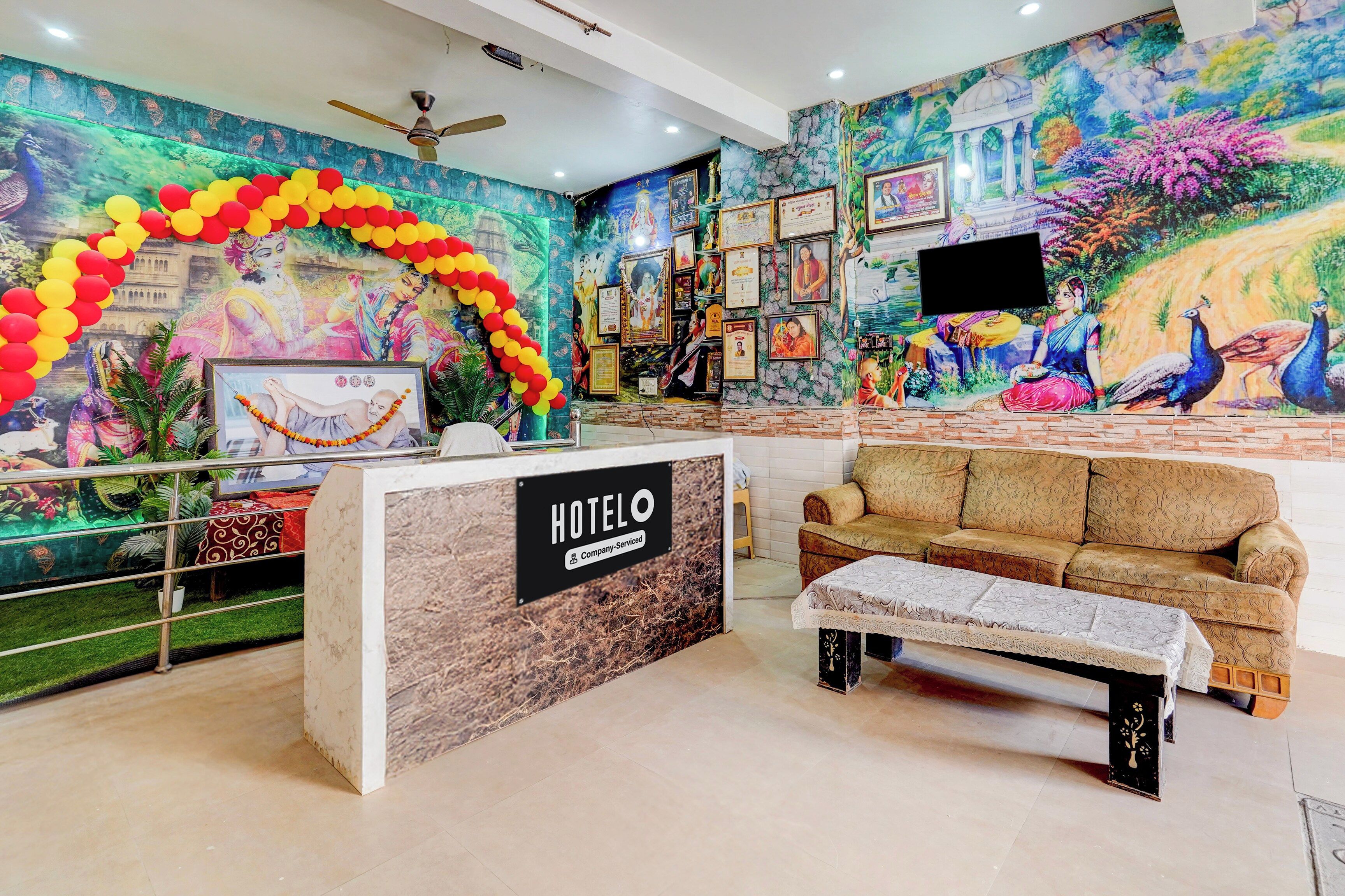 Uma área de recepção de hotel, com balcão, sofá e um mural com pavões.