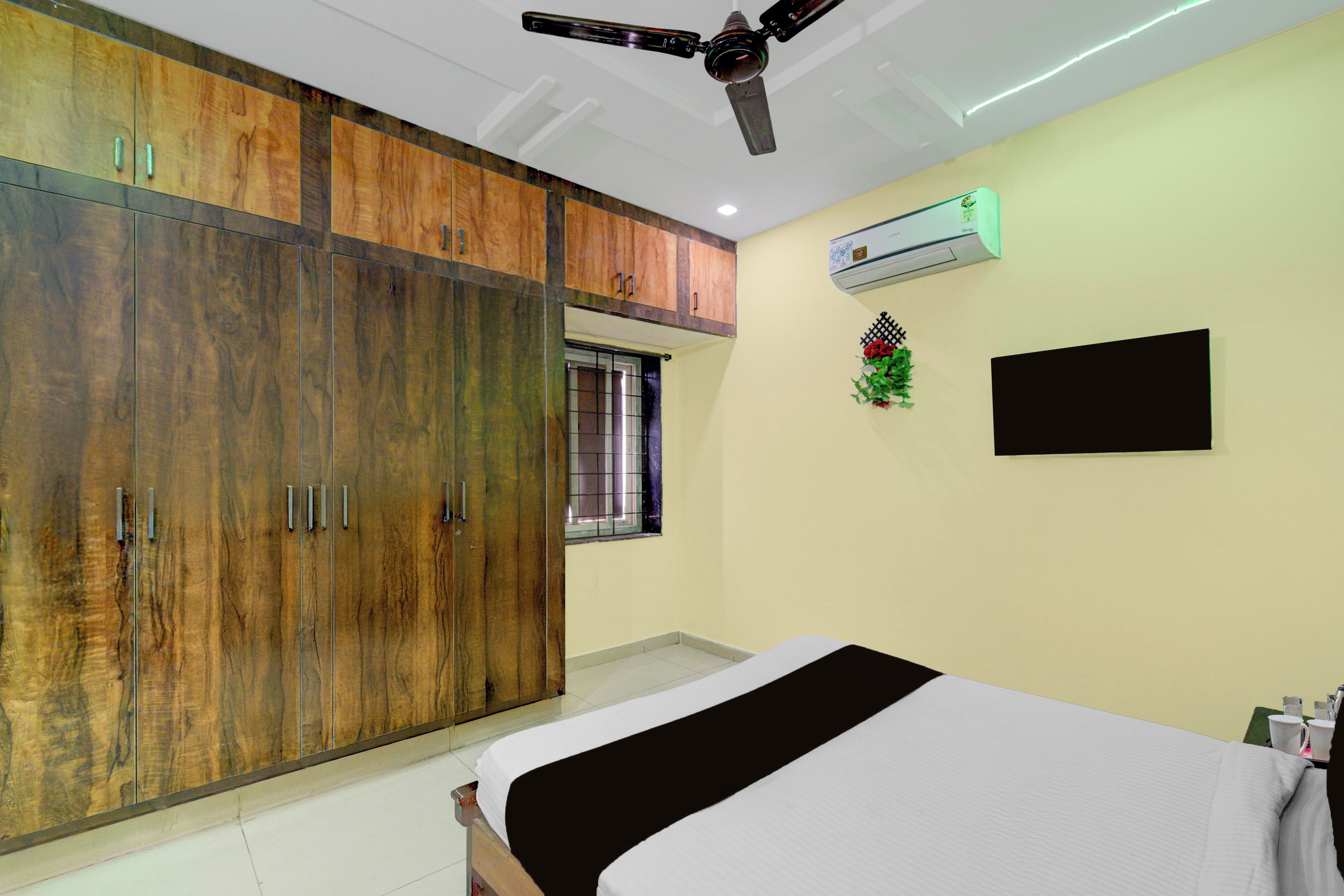 Quarto com cama, guarda-roupa, ventoinha no teto, ar condicionado e janela com vista.