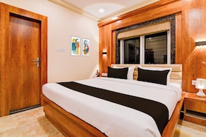 Quarto de hotel com cama, cabeceira de madeira, mesa de cabeceira com abajur e duas obras de arte penduradas na parede.