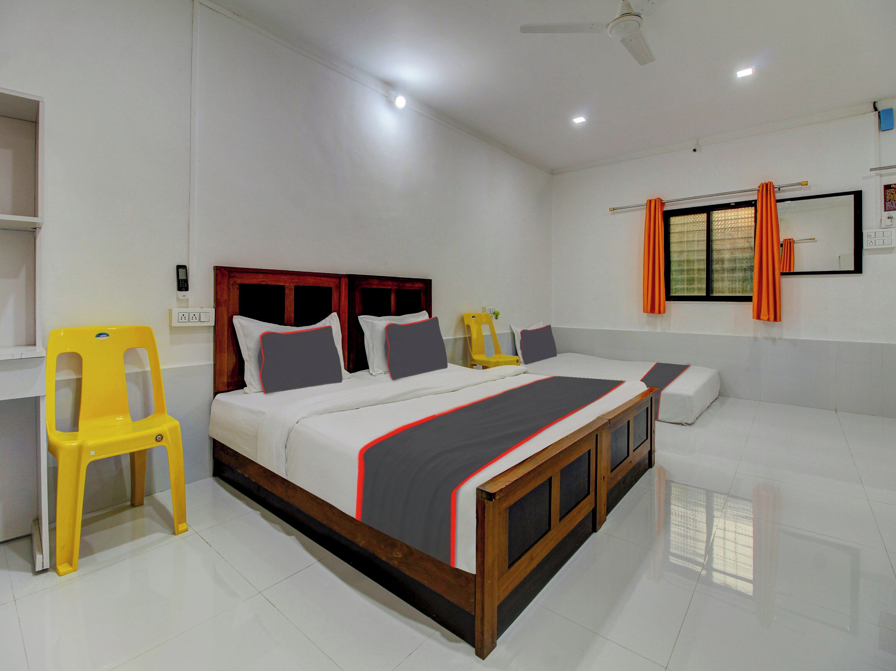 Quarto com cama, uma cadeira, mesa de cabeceira e janela com cortinas.