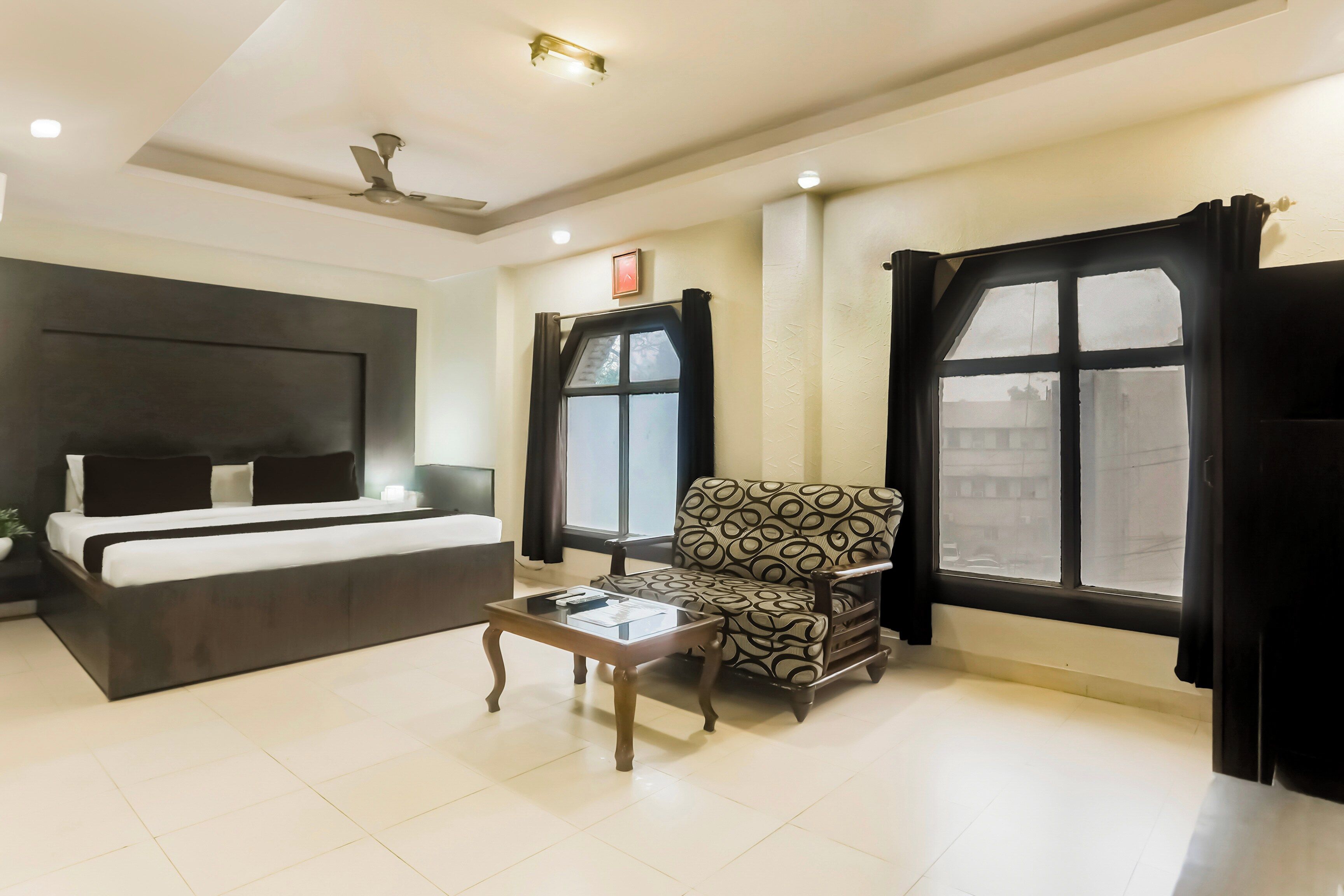 Quarto de hotel moderno com cama, sofá, mesa de centro e uma janela grande com cortinas.