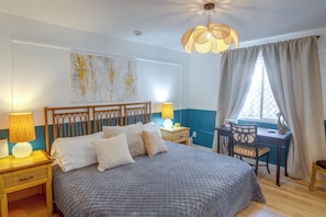 Quarto com cama, abajures, escrivaninha com cadeira e janela com cortinas.