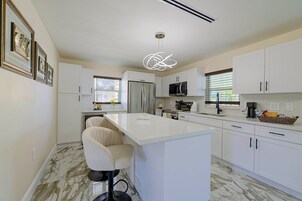 Cozinha moderna com armários brancos, piso de mármore, ilha central com banquetas e luminária pendente.