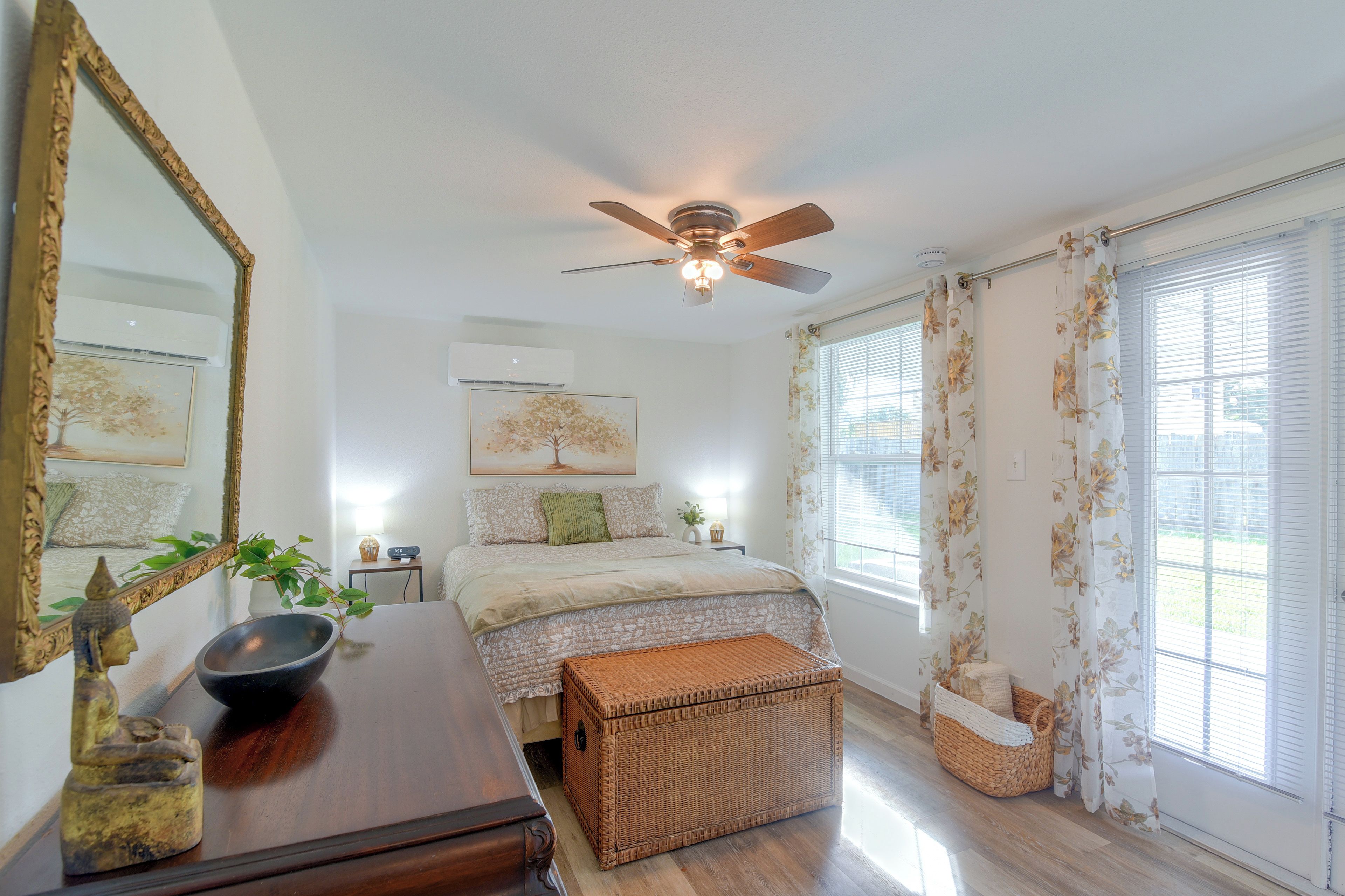 Quarto com cama, penteadeira, espelho, ventilador de teto e janela com cortinas.