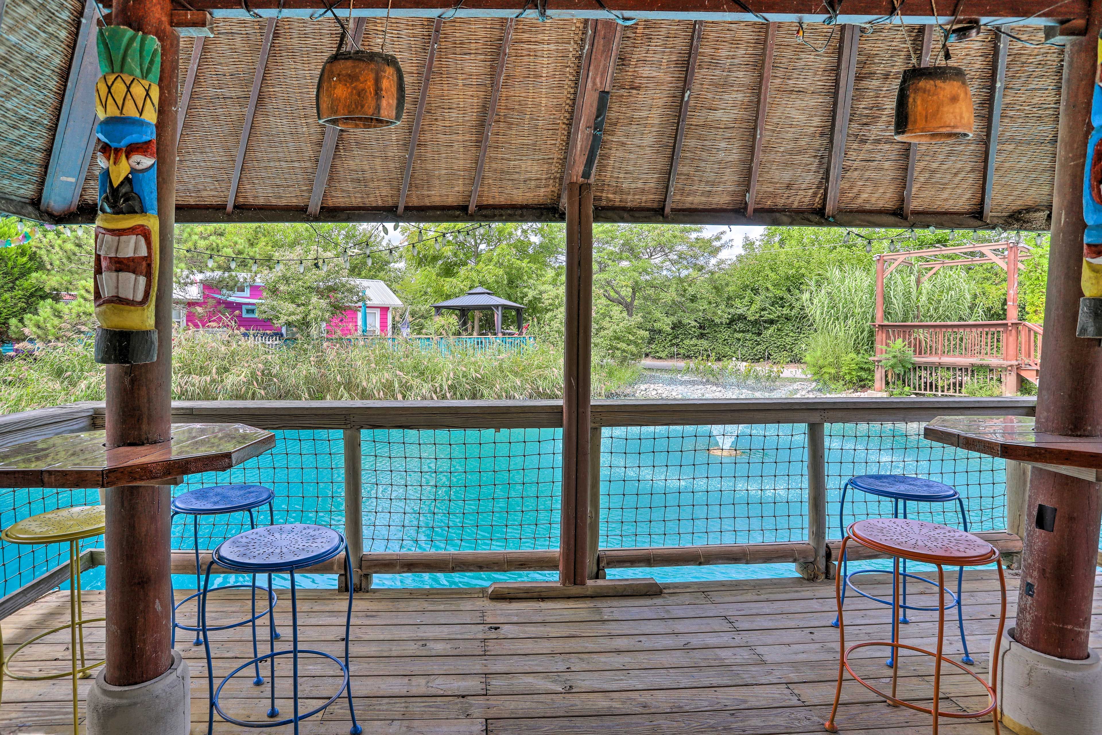 Um deck de madeira com piscina, cadeiras azuis e telhado de palha.