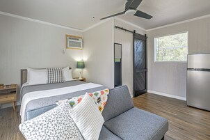Quarto moderno com cama, sofá, escrivaninha, luminária, ventilador de teto, janela e geladeira.