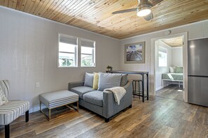 Uma sala de estar moderna com um sofá cinza, um banquinho listrado e um ventilador de teto.