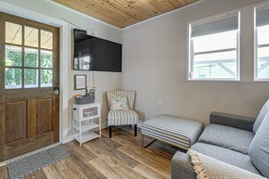 Uma sala de estar aconchegante com porta de madeira, televisão na parede, poltrona listrada, um banco e janela com persianas.