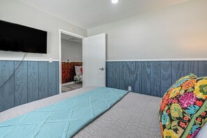 Quarto com uma cama, televisão fixada na parede e porta que dá para outro cômodo.