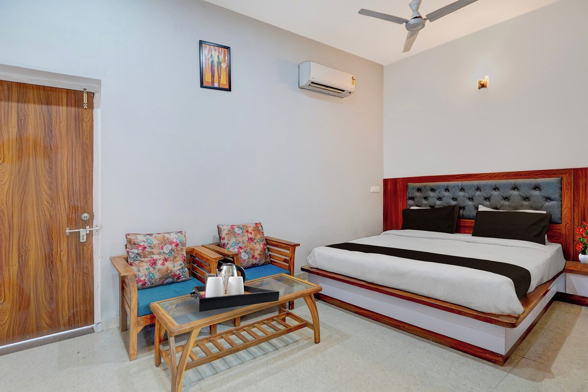 Quarto de hotel com uma cama, uma mesinha com bandeja, uma cadeira, um ventilador de teto e um ar condicionado.