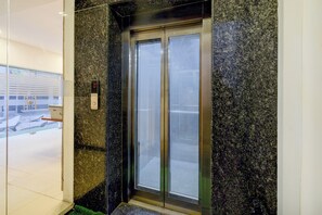 Um elevador com mostrador digital, paredes metálicas e porta de vidro.