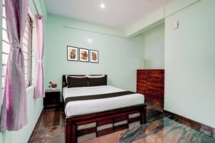 Quarto com cama, mesa de cabeceira, janela com cortinas e uma parede com três quadros emoldurados.