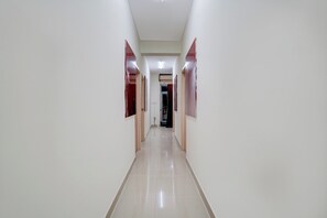 Um corredor comprido e estreito, com paredes brancas e chão de azulejos brilhantes.