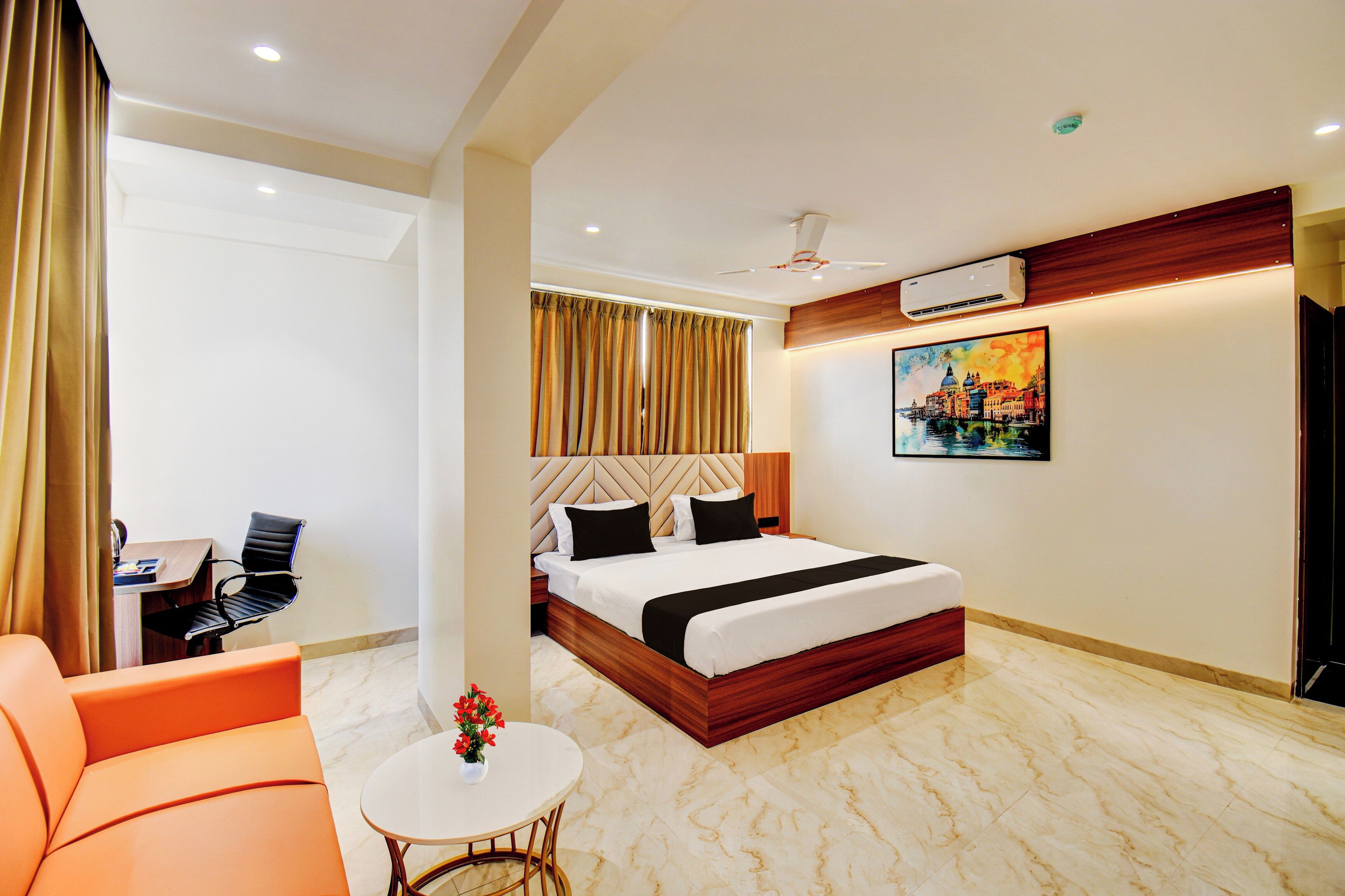 Quarto de hotel com cama, escrivaninha, cadeira, pequena mesa com flores e um quadro na parede.