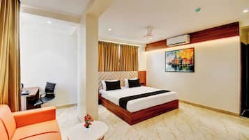 Quarto de hotel com cama, escrivaninha, cadeira, pequena mesa com flores e um quadro na parede.