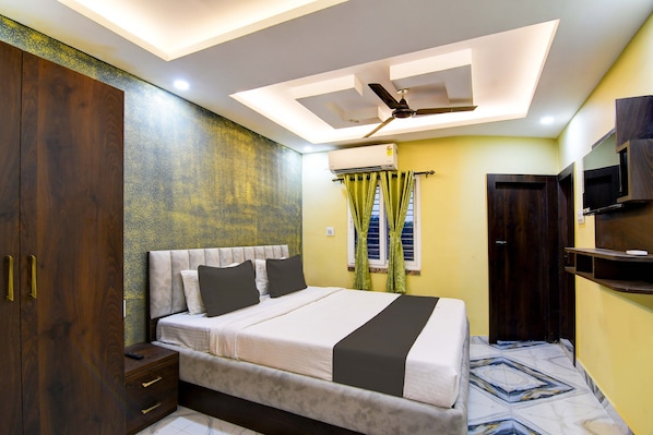 Quarto com cama, guarda-roupa, ventoinha no teto, aparelho de ar condicionado, televisão e janela com cortinas.