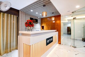 Balcão de recepção com uma placa indicando 'OYO' e um arranjo floral decorativo.