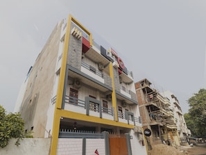 Um edifício com vários andares, fachada amarela e branca, varandas e uma porta visível.