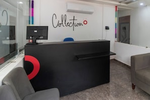 Bancada de recepção com balcão preto, um monitor de computador e um telefone fixado na parede.