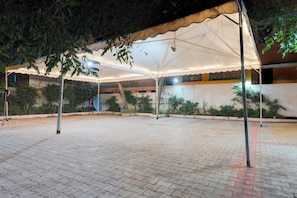 Área externa coberta com piso de azulejos, cercada por vegetação e um edifício com um mural.