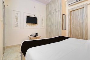 Quarto de hotel com cama, televisão na parede, guarda-roupa e uma pequena mesa com chaleira e chávenas.
