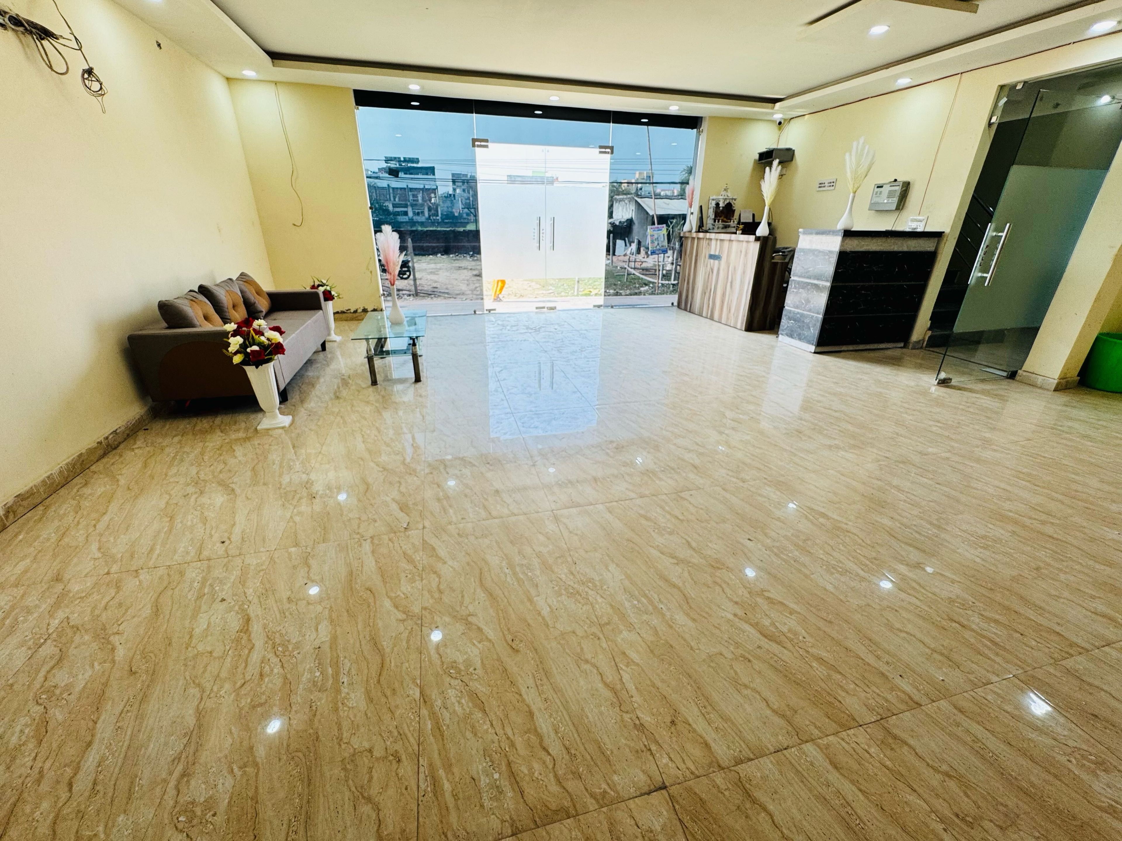 Um hall espaçoso com piso de mármore, um sofá com almofadas, uma mesa de vidro e vista para o exterior através de uma porta de vidro.