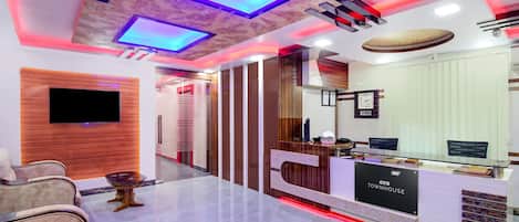 Uma área de recepção com design moderno, incluindo balcão, espaço para assentos e uma TV de tela plana na parede.