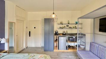 Quarto compacto com cama, sofá, cozinha compacta e área de jantar.
