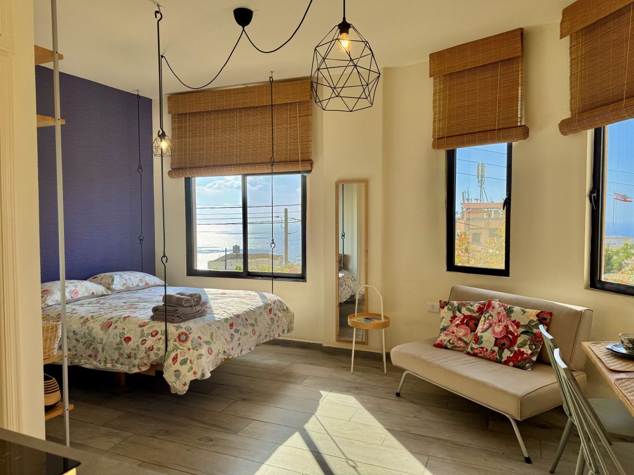 Quarto com cama, sofá, poltrona, espelho e janela com vista.